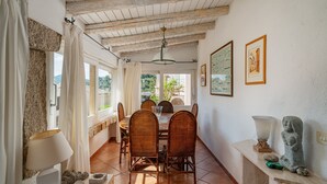Uma sala de jantar com mesa e cadeiras de madeira, luminária pendente e quadros nas paredes.