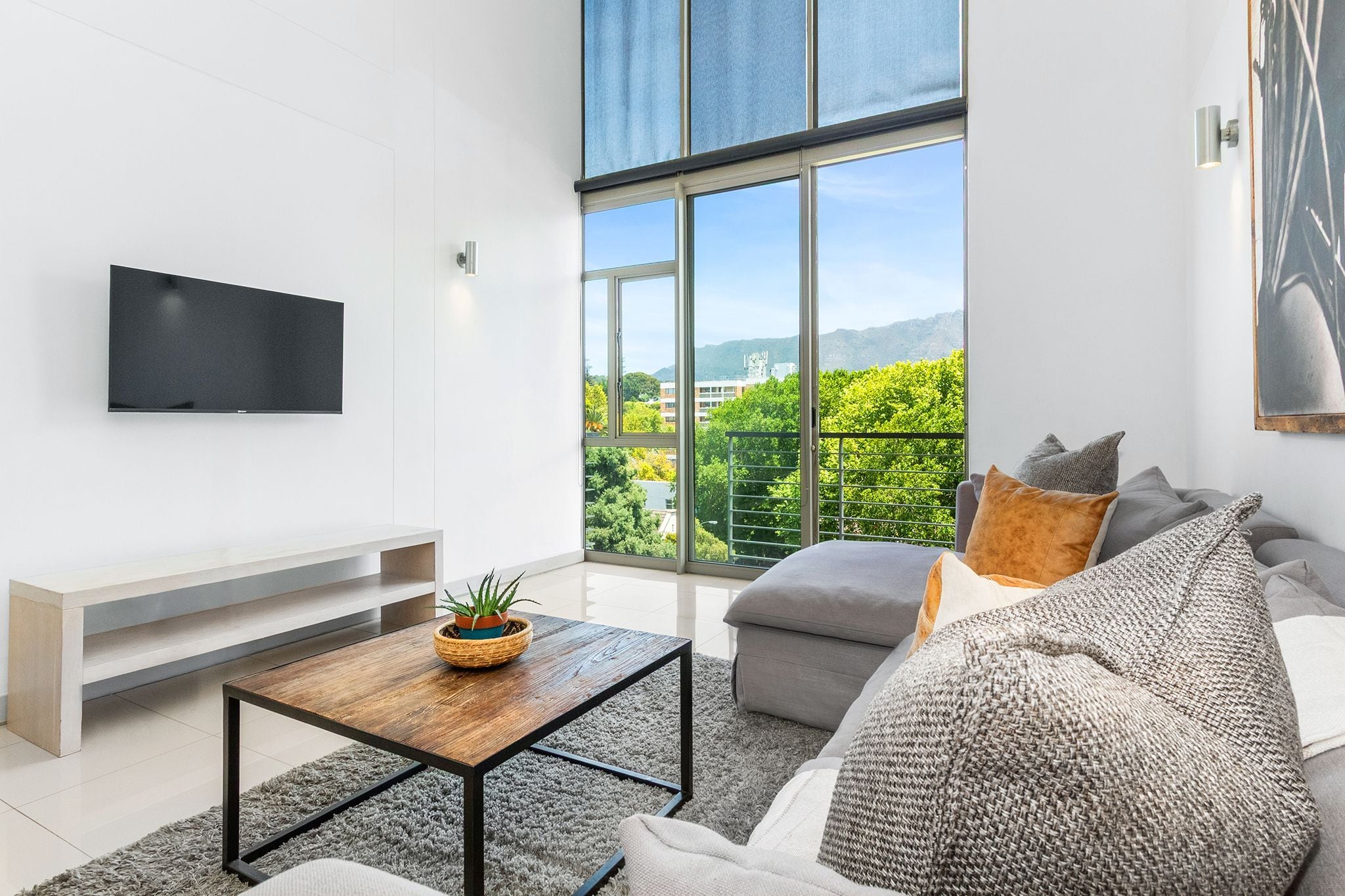 Uma sala de estar moderna, com uma janela grande, uma TV de tela plana, um sofá e uma mesa de centro.