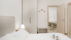 Quarto de hotel minimalista com uma cama, mesa de cabeceira e um pequeno espaço de estar.