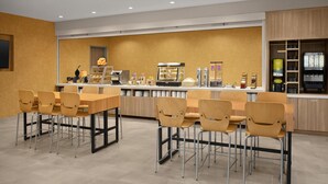 Um café moderno com mesas e cadeiras de madeira, um balcão com diversos alimentos e uma vitrine.