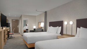 Quarto de hotel com duas camas, uma mesa, uma cadeira, uma televisão e uma luminária.