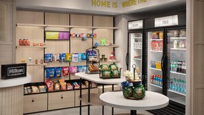 Espaço de exposição com diversos lanches embalados, uma área refrigerada e um aviso indicando a localização dos snacks.