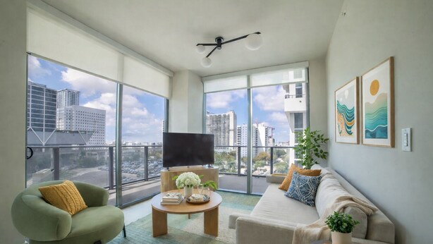 Sala de estar moderna com sofá, poltrona, mesa de centro e televisão. Janelas amplas proporcionam vista para a cidade.