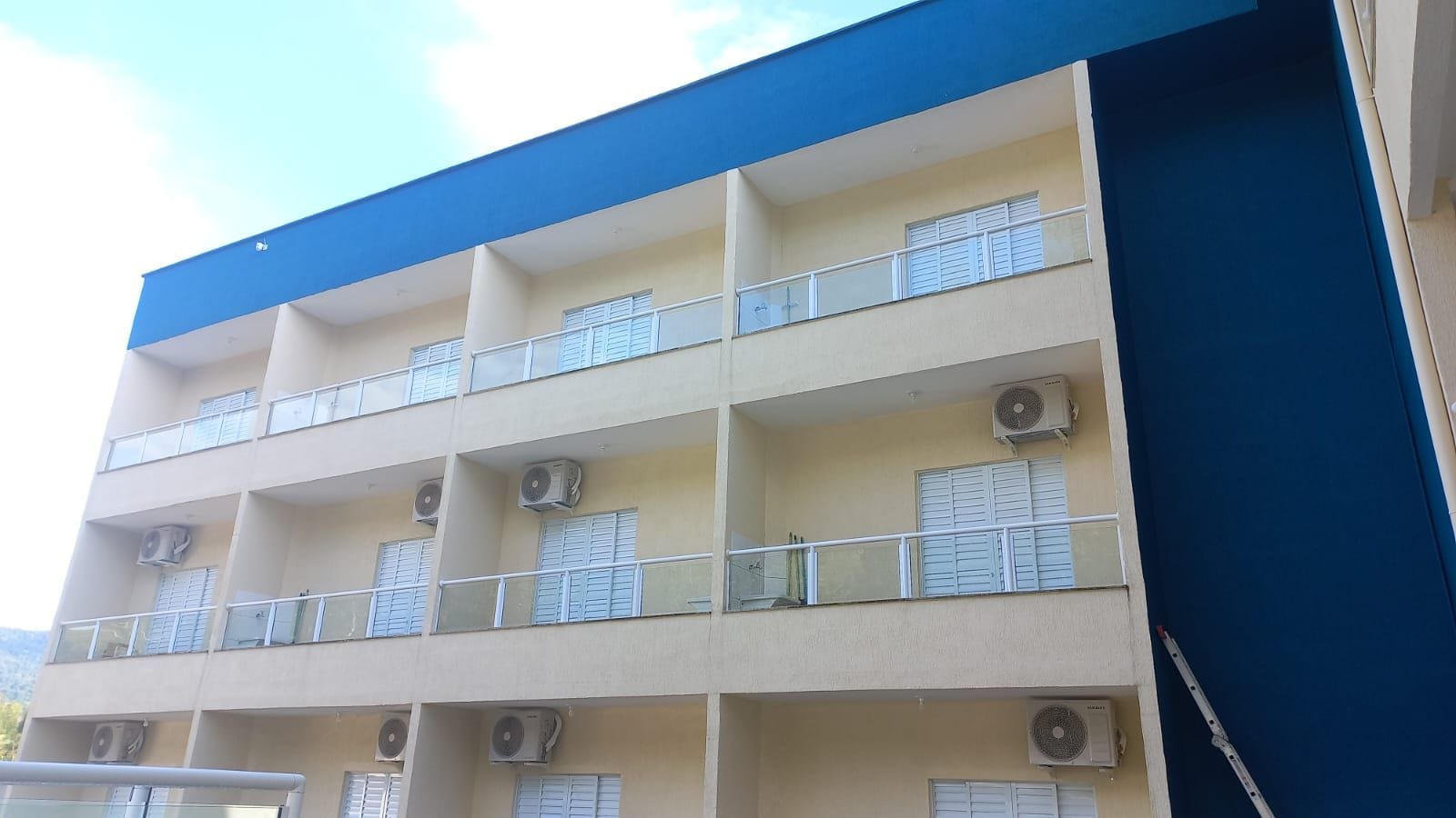 Edifício com várias andares, varandas, aparelhos de ar condicionado e toldo azul.