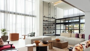 Uma sala de estar ampla com uma janela grande, um sofá moderno, uma mesa de centro e uma estante de livros.