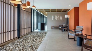 Um hall de hotel moderno, com balcão de recepção, área de estar e um caminho decorativo com pedrinhas.