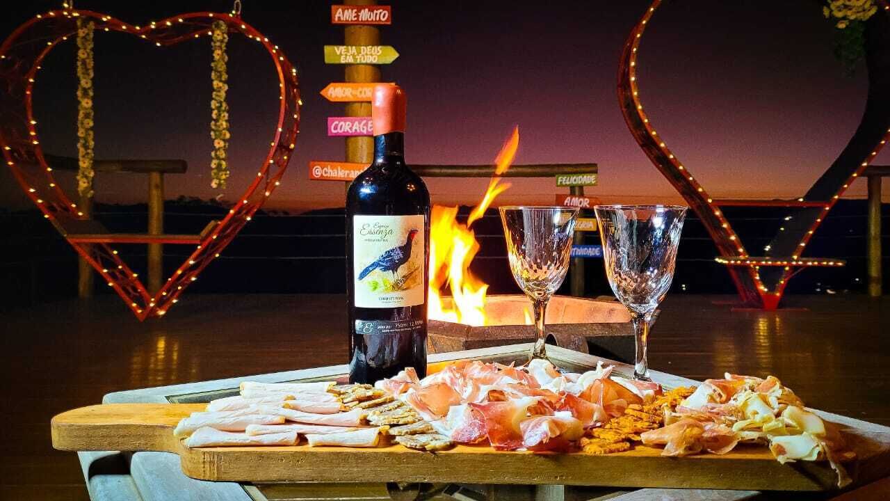 Uma mesa com uma garrafa de vinho, dois copos e diversos tipos de carne.