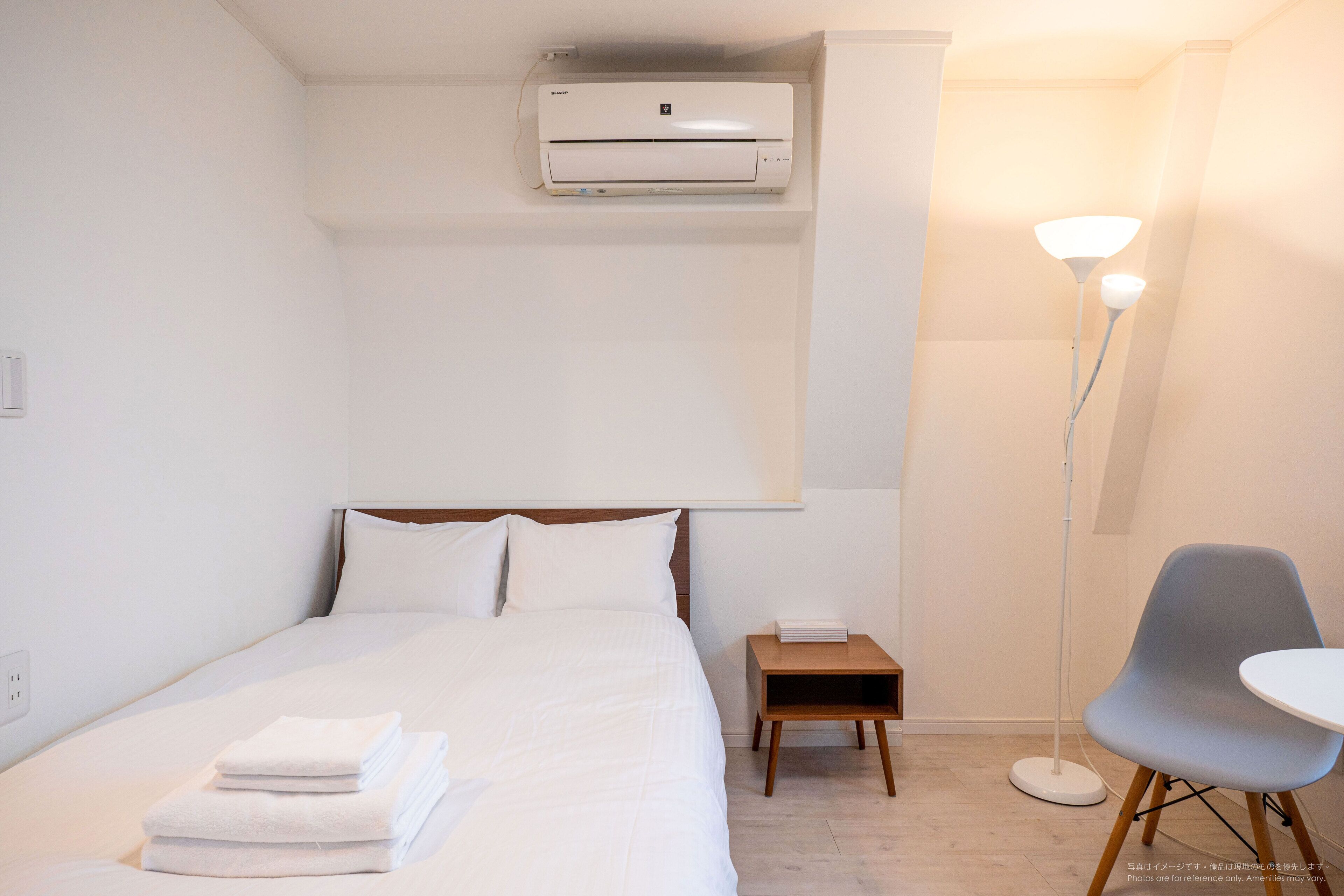 Quarto de hotel com cama, mesa de cabeceira, luminária e ar condicionado.