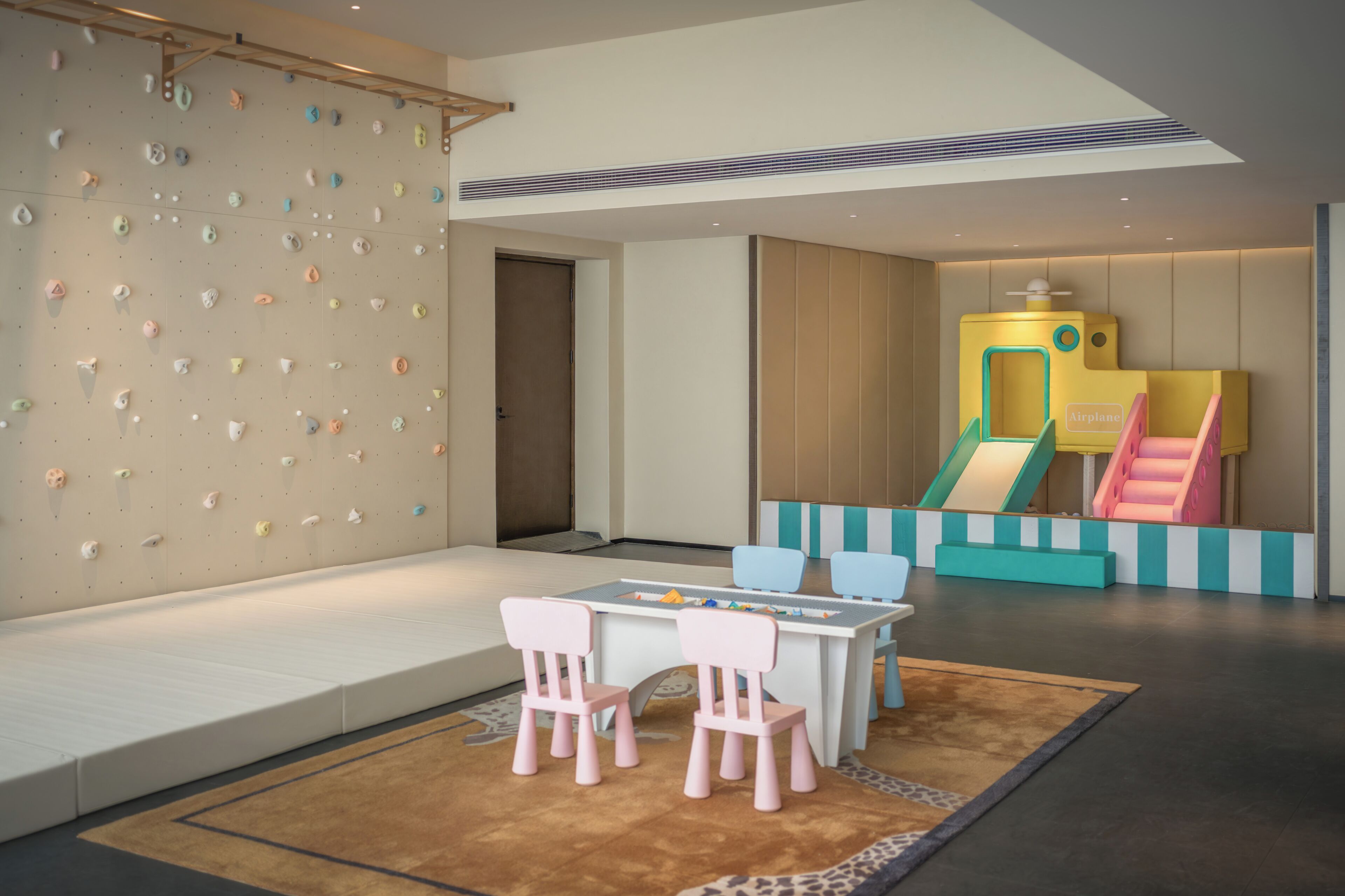 Uma área de recreação infantil com paredes de escalada, um escorrega e uma mesa com cadeiras.