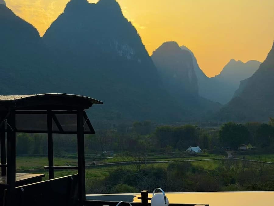 Terraço com vista para montanhas ao pôr do sol, uma mesa e dois objetos brancos esféricos.