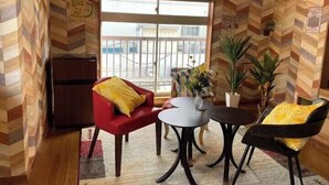 Um quarto com teto de madeira em padrão geométrico Chevron, uma cadeira vermelha com almofada amarela, uma pequena mesa redonda com um vaso de flores, e uma cadeira preta com almofada amarela.