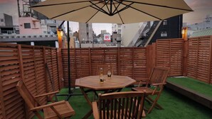Um terraço no terraço com uma mesa redonda e quatro cadeiras de madeira, cercado por uma cerca de madeira e um grande guarda-sol.