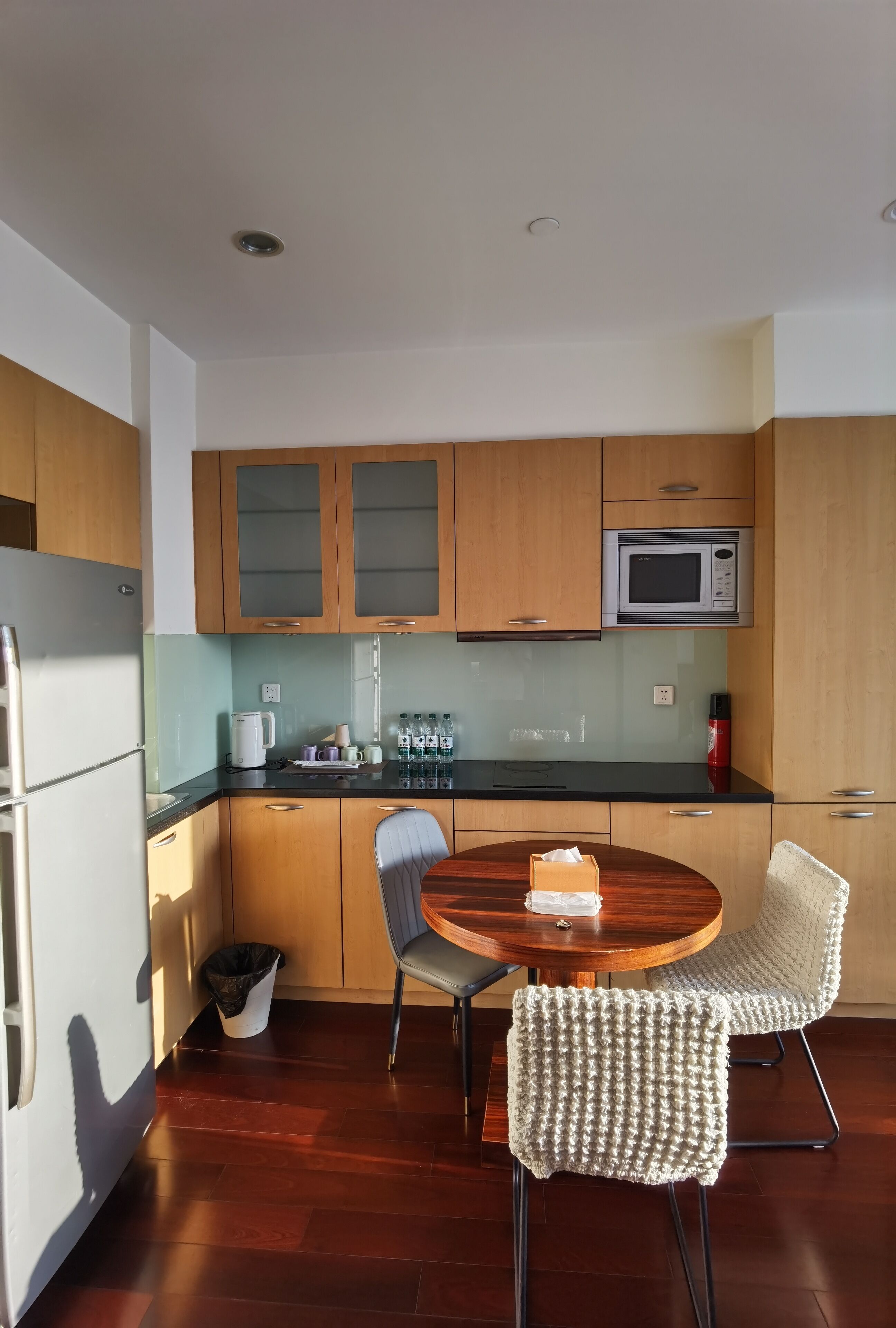 Cozinha moderna com armários de madeira, micro-ondas e uma mesa de jantar redonda com duas cadeiras.
