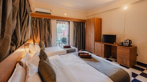 Quarto de hotel com duas camas, televisão, mesa com cafeteira e varanda com cortinas.