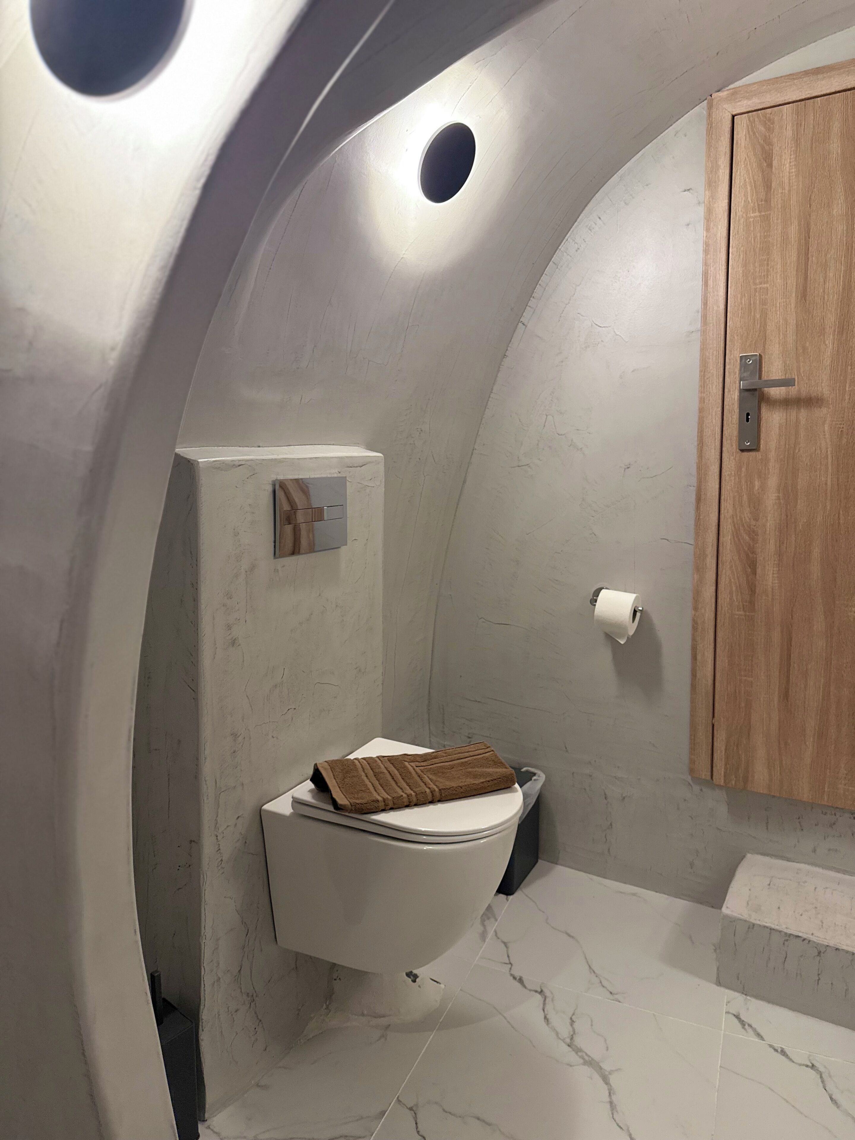 Um banheiro compacto e curvo com vaso sanitário, um armário de madeira e piso de mármore.