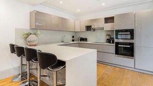 Cozinha moderna com ilha central, banquetas de bar, eletrodomésticos de aço inoxidável e armários em tons claros.