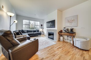 Uma sala de estar moderna com sofá de couro, lareira, mesa de centro e área de jantar com mesa e cadeiras de madeira.