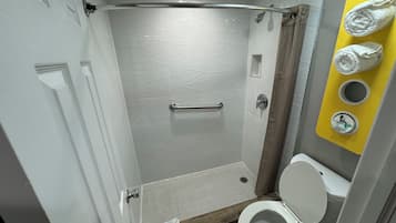 Casa de banho com chuveiro, sanita e porta-toalhas com toalhas.