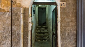 Uma porta estreita e em arco dá acesso a um corredor pouco iluminado com escadas.
