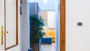 Um corredor com uma porta de madeira, um vaso azul e um sofá amarelo ao fundo.