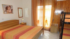 Quarto de hotel com uma cama grande, uma mesa de cabeceira com abajur, espelho e janela com cortinas.