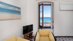 Quarto com vista para a praia, televisão e duas cadeiras amarelas.