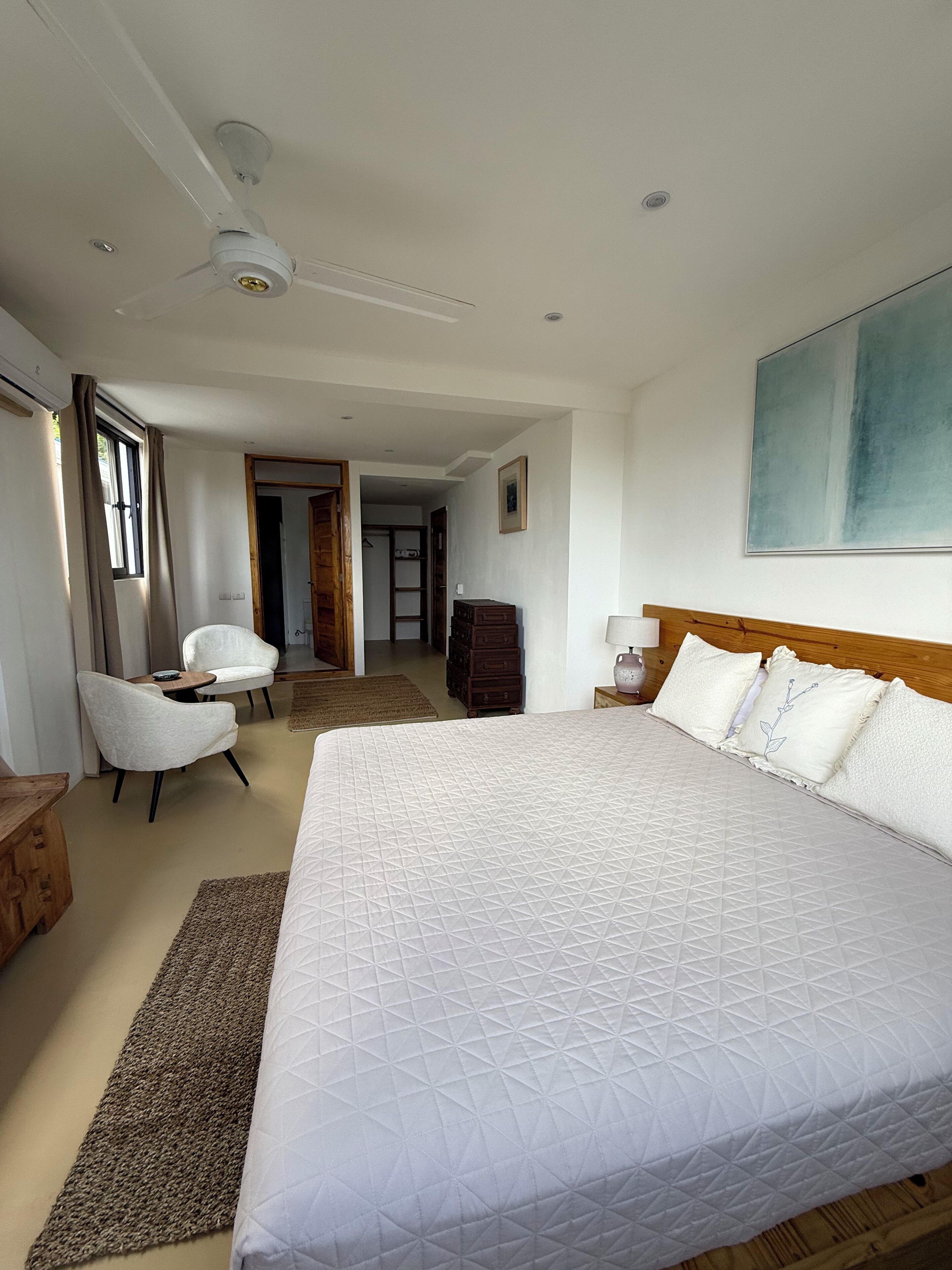 Quarto de hotel com uma cama grande, uma escrivaninha, uma cadeira, um guarda-roupa e um ventilador de teto.