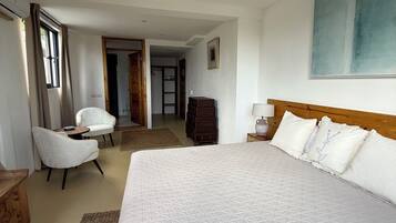 Quarto de hotel com uma cama grande, uma escrivaninha, uma cadeira, um guarda-roupa e um ventilador de teto.
