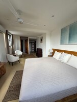 Quarto de hotel com uma cama grande, uma escrivaninha, uma cadeira, um guarda-roupa e um ventilador de teto.
