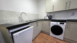 Uma cozinha compacta com lava-louças, máquina de lavar e uma pia com torneira moderna.