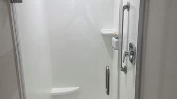 Box de chuveiro com paredes de azulejos brancos, chuveiro manual e uma toalha pendurada na porta.