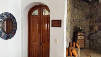 Uma porta de madeira com um painel de vidro, um espelho fixado na parede, uma placa emoldurada, uma parede de pedra, um sofá de vime com almofadas e um chão de azulejos.