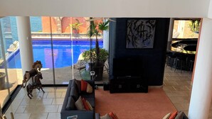 Sala de estar com sofá, mesa de centro e rack para TV. Piscina visível pelas portas de vidro.