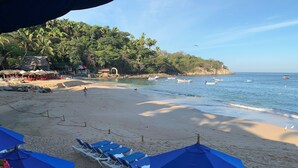 Uma praia com cadeiras de praia e guarda-sóis, uma faixa de areia e barcos na água.