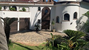 Um edifício com fachada branca, uma cúpula e um pátio com piso de pedra e palmeiras.