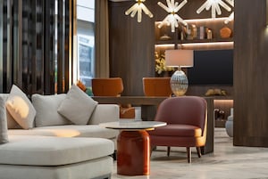 Uma sala de estar moderna com sofá, poltrona e mesa de centro, destacando um abajur exclusivo e uma televisão ao fundo.