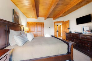Quarto com cama grande, cabeceira de madeira, cômoda e televisão de tela plana na parede.