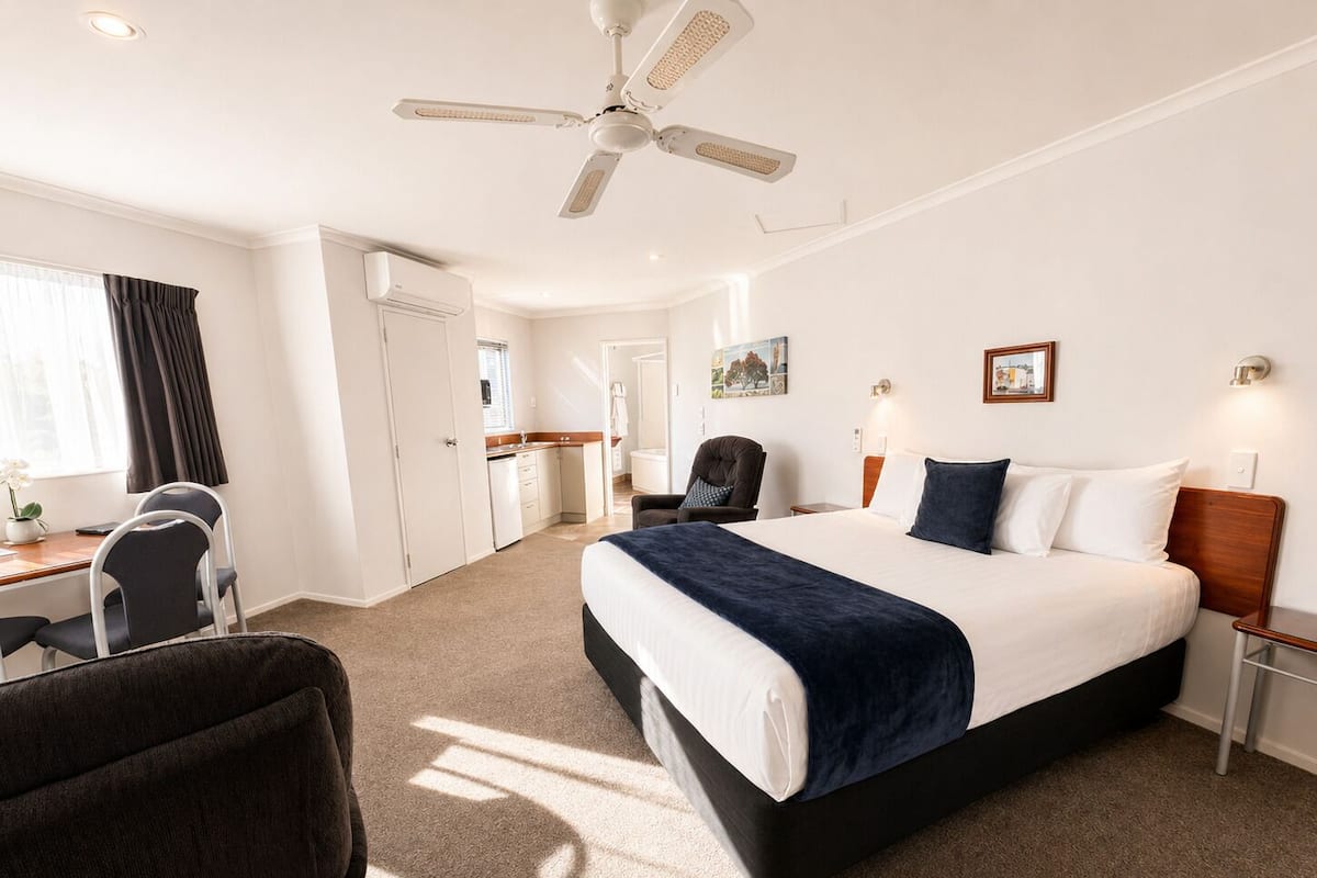Quarto de hotel com cama, escrivaninha, cadeira, ventilador de teto e obras de arte nas paredes.