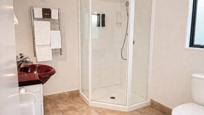 Uma casa de banho moderna com cabine de duche em vidro, toucador com lavatório vermelho e sanita.