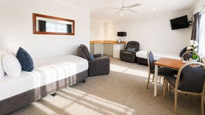 Quarto de hotel com cama, duas poltronas, uma mesinha, televisão, ventoinha no teto e uma cozinha compacta.