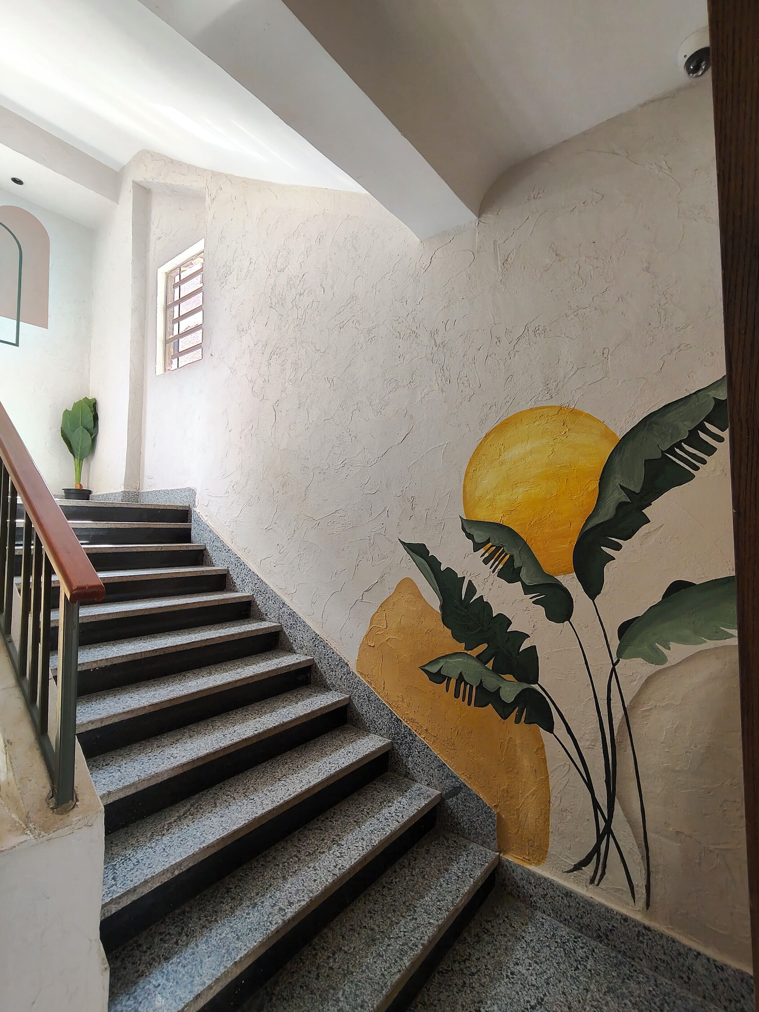 Uma escadaria com um mural pintado à mão de um sol e folhagem na parede.