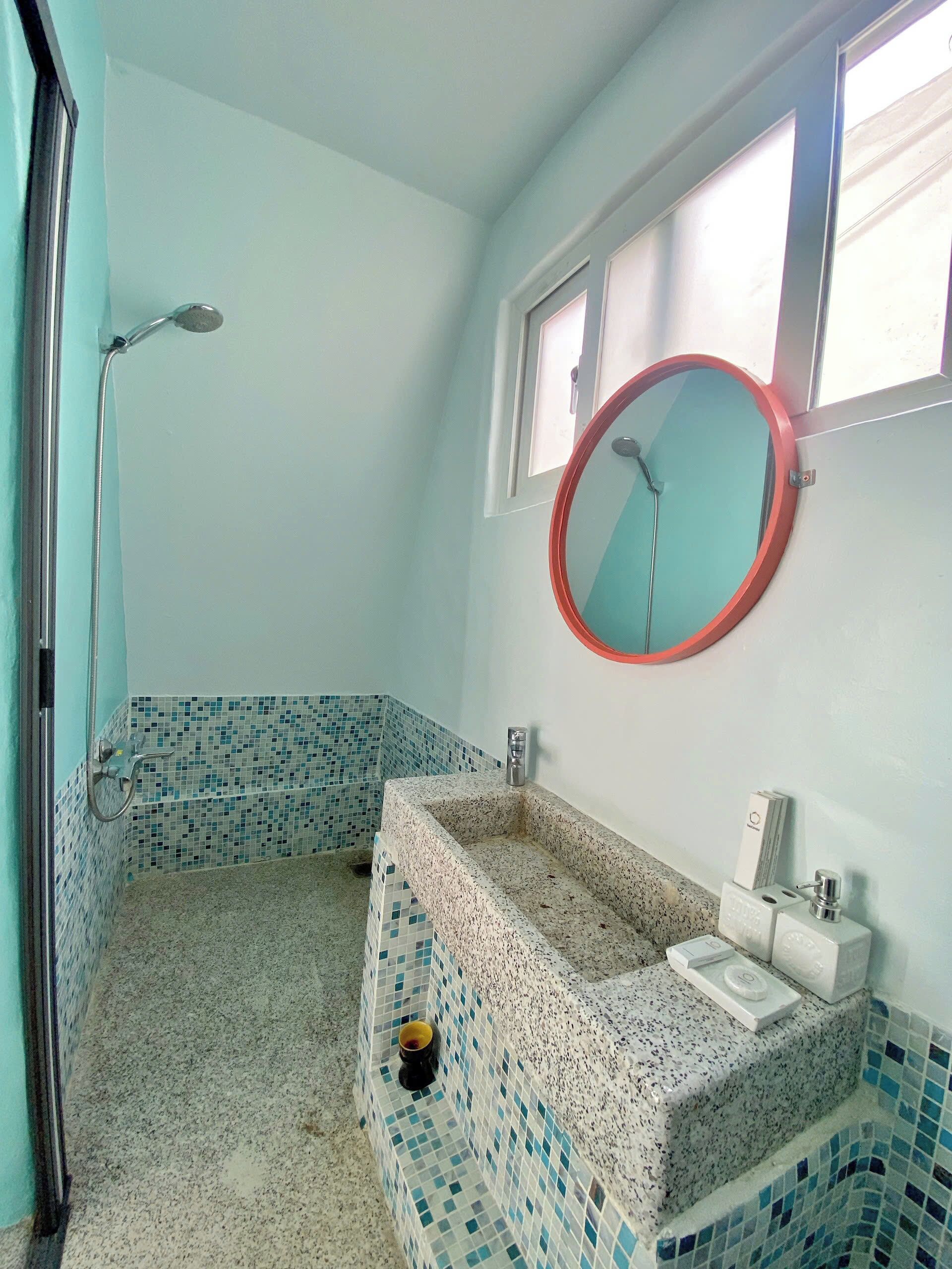 Casa de banho com chuveiro, lavatório com espelho e paredes em azulejo.