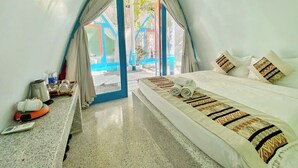 Um quarto acolhedor com uma cama, uma mesinha com uma chaleira e uma xícara, e vista para uma área externa colorida.