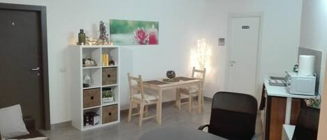 Um quarto com uma mesa de jantar, cadeiras, um armário branco com prateleiras, um quadro e uma porta.