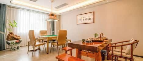 Uma área de refeições com mesa de madeira, cadeiras e um banco. Há uma planta à esquerda e um quadro na parede.
