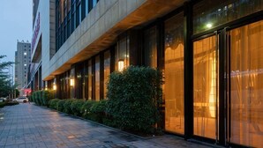 Exterior moderno de hotel com janelas amplas, calçada pavimentada e sebe bem cuidada.
