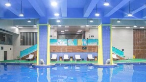 Uma piscina interior com várias pistas de natação, espreguiçadeiras e uma parede revestida com um mural.
