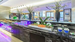 Um hall de hotel com uma receção em mármore, plantas em vasos e vista para a cidade.