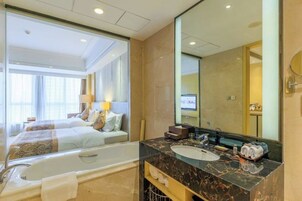 Quarto de hotel com uma cama grande, uma banheira, toucador de mármore e um espelho amplo.