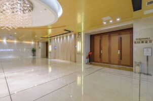 Um saguão de hotel com piso lustroso, balcão de recepção e uma grande porta de madeira com a inscrição 'SHIJIAHALL'.